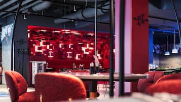 Um interior moderno com uma área de estar vermelha, um bar com painéis vermelhos iluminados e dutos expostos no teto.