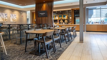 Um restaurante com várias mesas e cadeiras, uma tela de televisão e uma área de cozinha com diversos itens expostos.