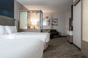 Quarto de hotel com duas camas, um espaço de estar, uma televisão e um banheiro visível através de uma porta aberta.