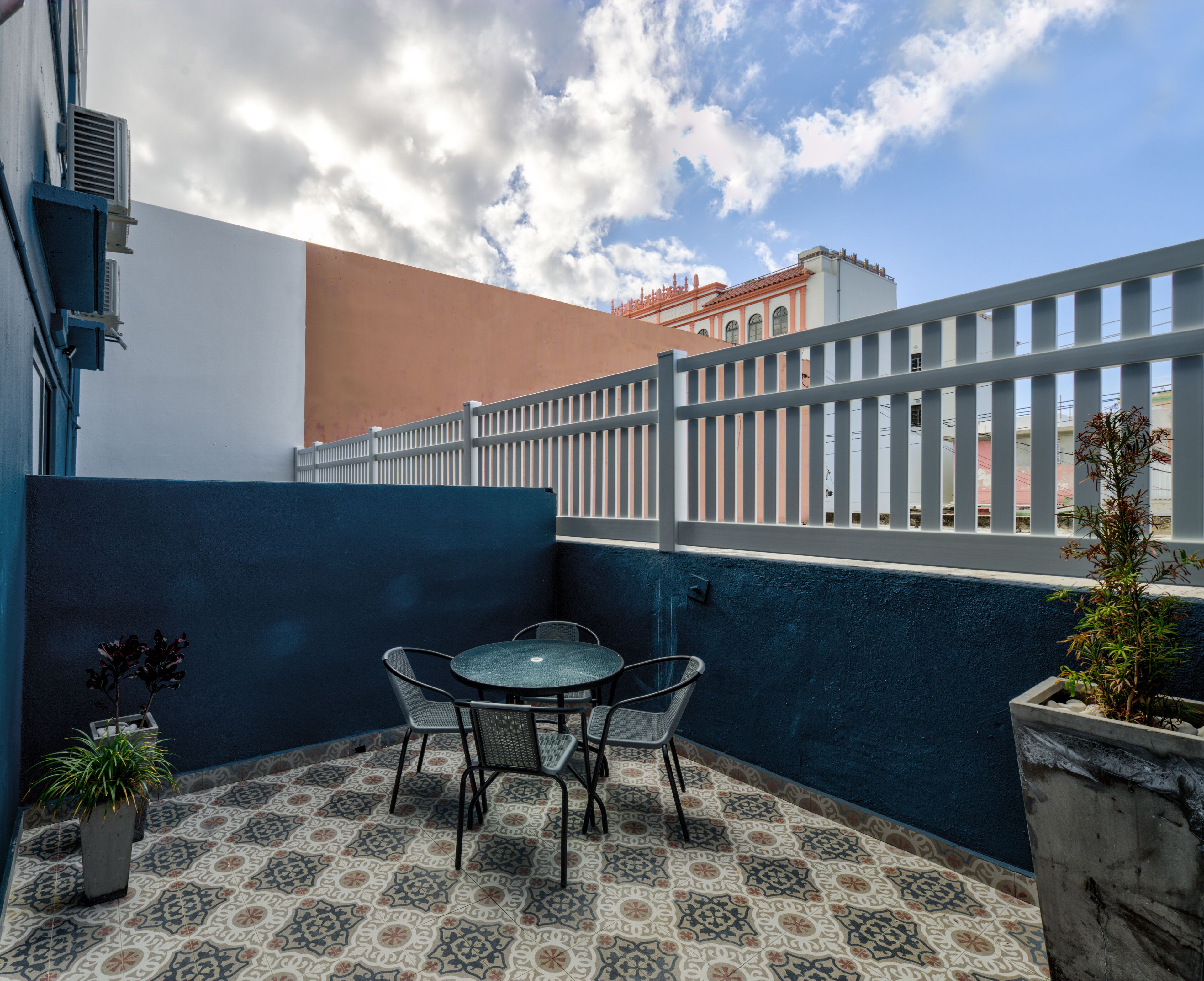 Um terraço no telhado com mesa e cadeiras, um vaso de planta e vista para um edifício ao fundo.