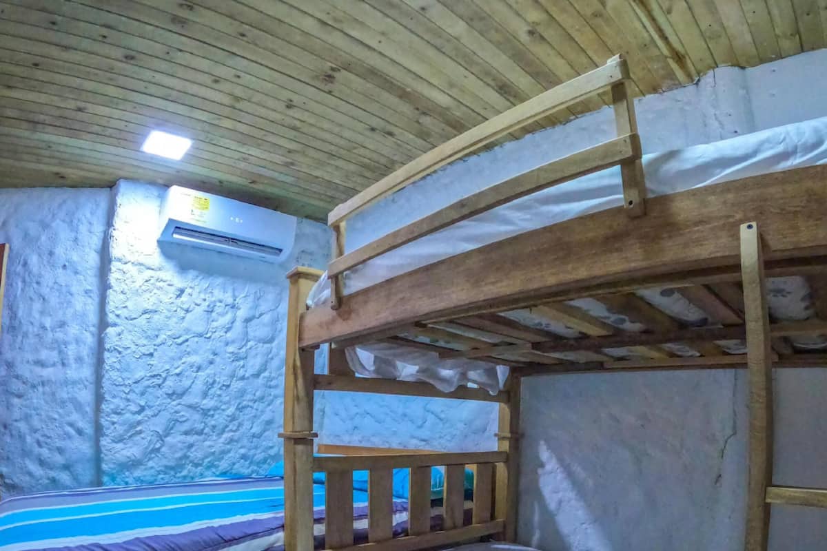 Quarto com beliche, teto de madeira e uma cama simples com manta listrada.