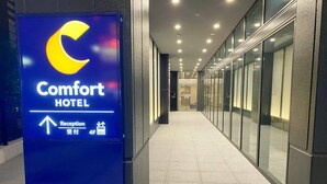 Um sinal azul do Comfort Hotel com o logotipo de uma crescente lunar, indicando que a recepção fica à frente.