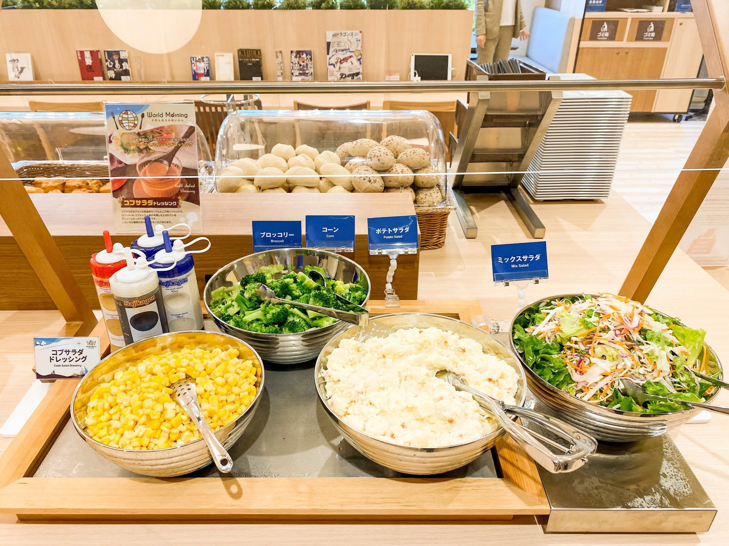 Buffet com diversas opções de comida, incluindo milho, salada de batata, brócolis e salada mista.