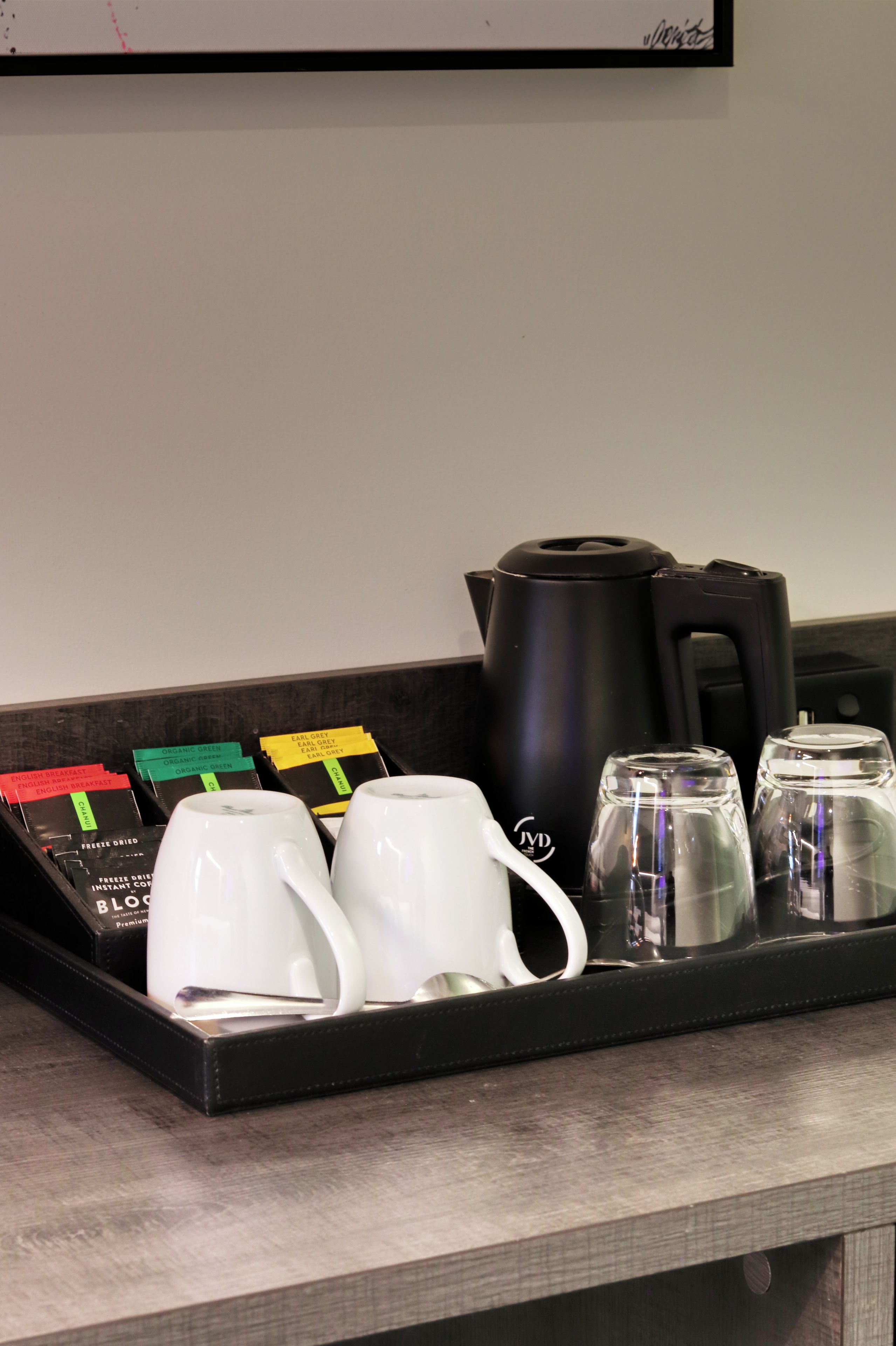 Estação de café com cafeteira preta, duas canecas brancas e bandeja com cápsulas de café.