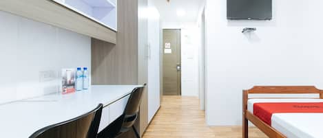 Quarto de hotel com uma cama, uma escrivaninha com cadeiras, uma televisão fixada na parede e um dispensador de água na escrivaninha.