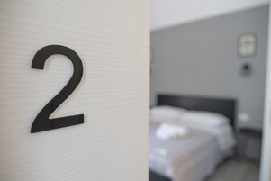 Quarto de hotel com o número 2 grande na parede, uma cama, uma mesa de cabeceira e um quadro na parede.