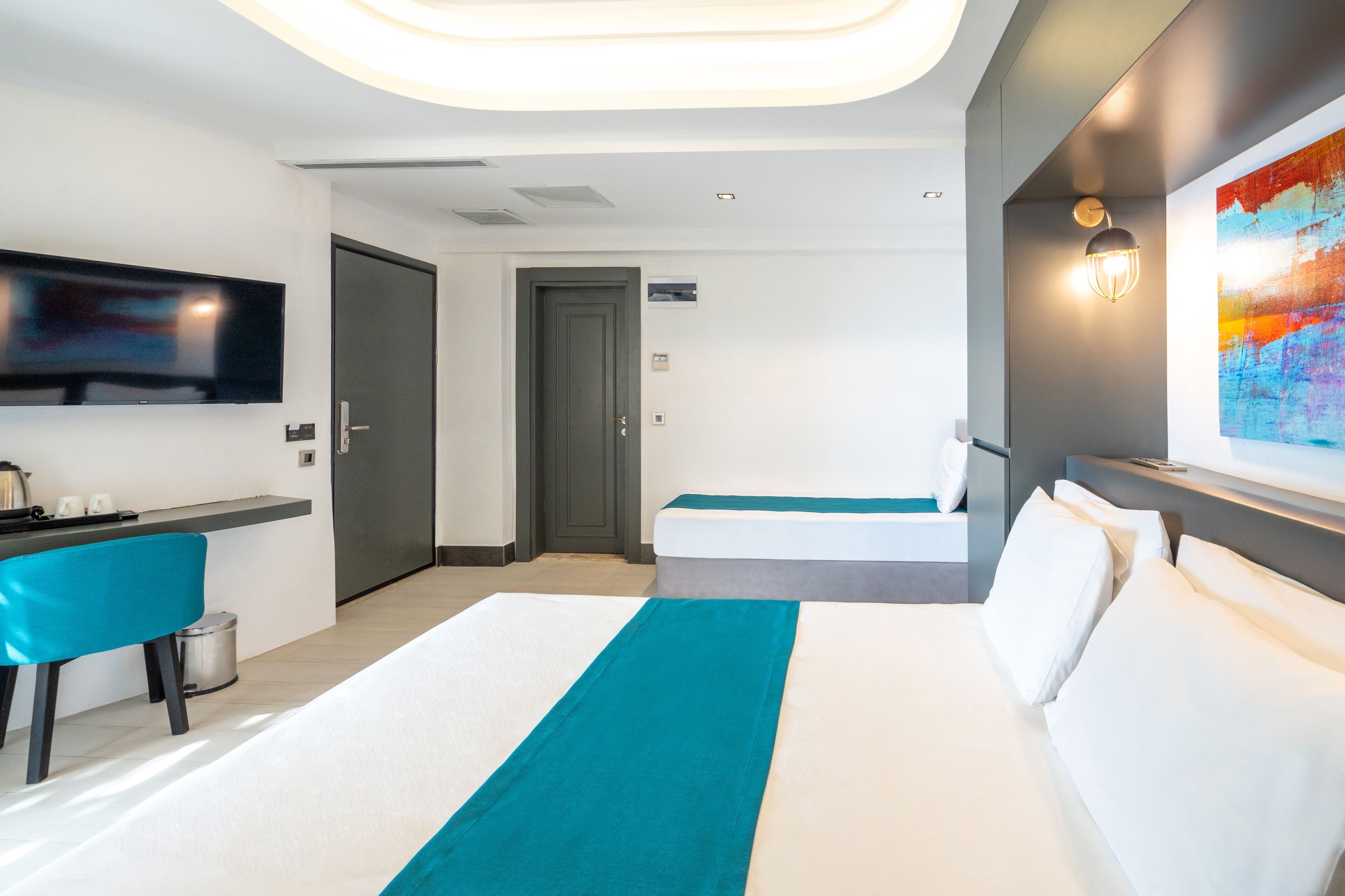 Quarto de hotel moderno com uma cama grande, uma escrivaninha com cadeira, televisão e um quadro na parede.