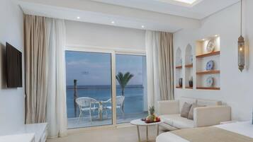 Quarto de hotel moderno com varanda, sofá, uma pequena mesa com frutas e prateleiras decorativas.