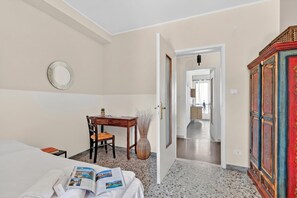 Quarto de hotel com cama, escrivaninha, cadeira, vaso e guarda-roupa.