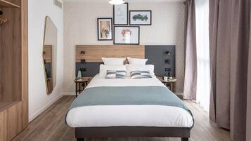 Quarto moderno com uma cama grande, cabeceira de madeira, mesas de cabeceira e quadros nas paredes.