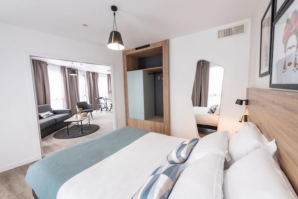 Quarto de hotel moderno com uma cama grande, um sofá, uma mesa de jantar e um espelho.