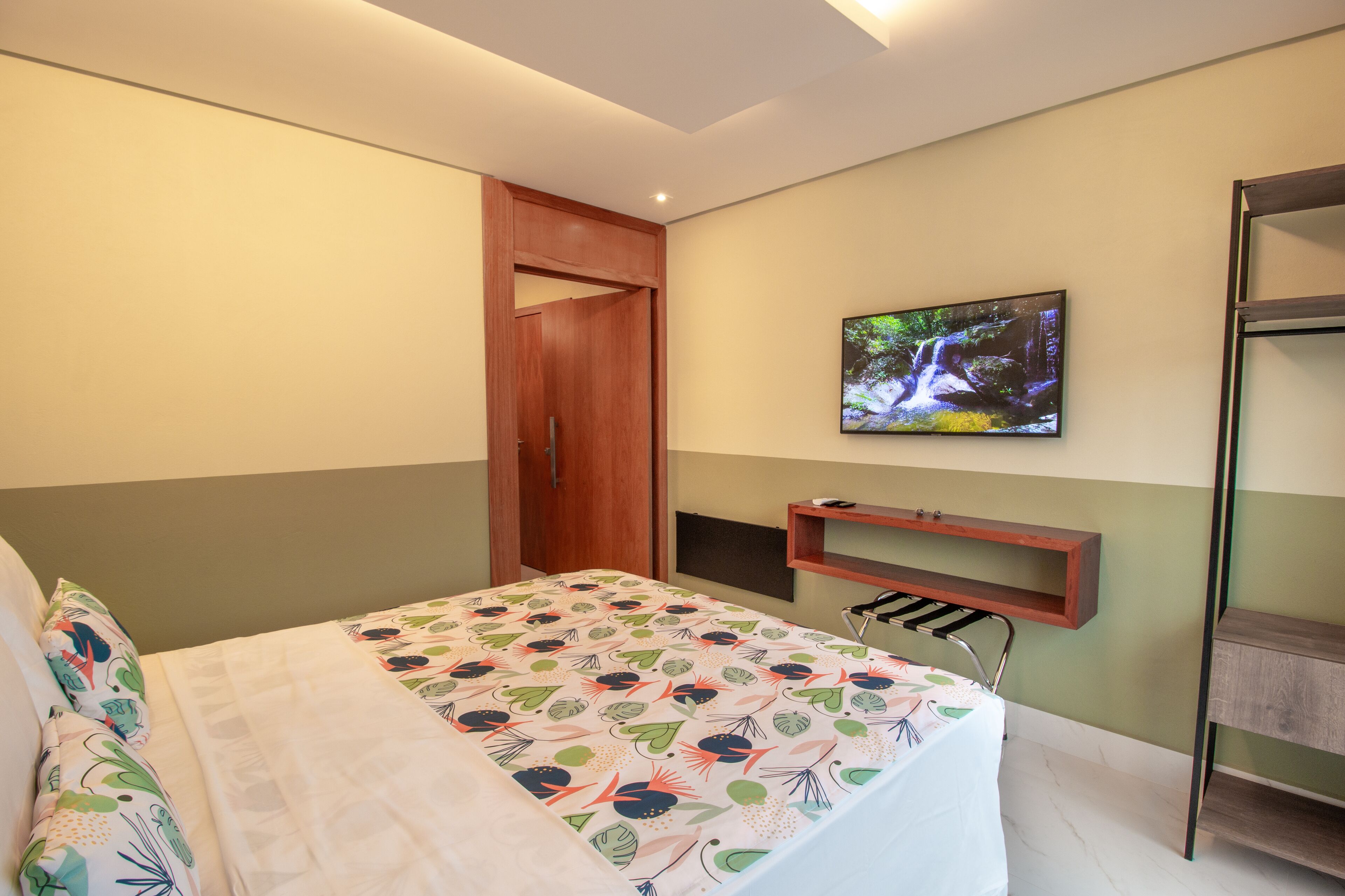 Quarto com cama, televisão na parede, porta de madeira e uma estante.
