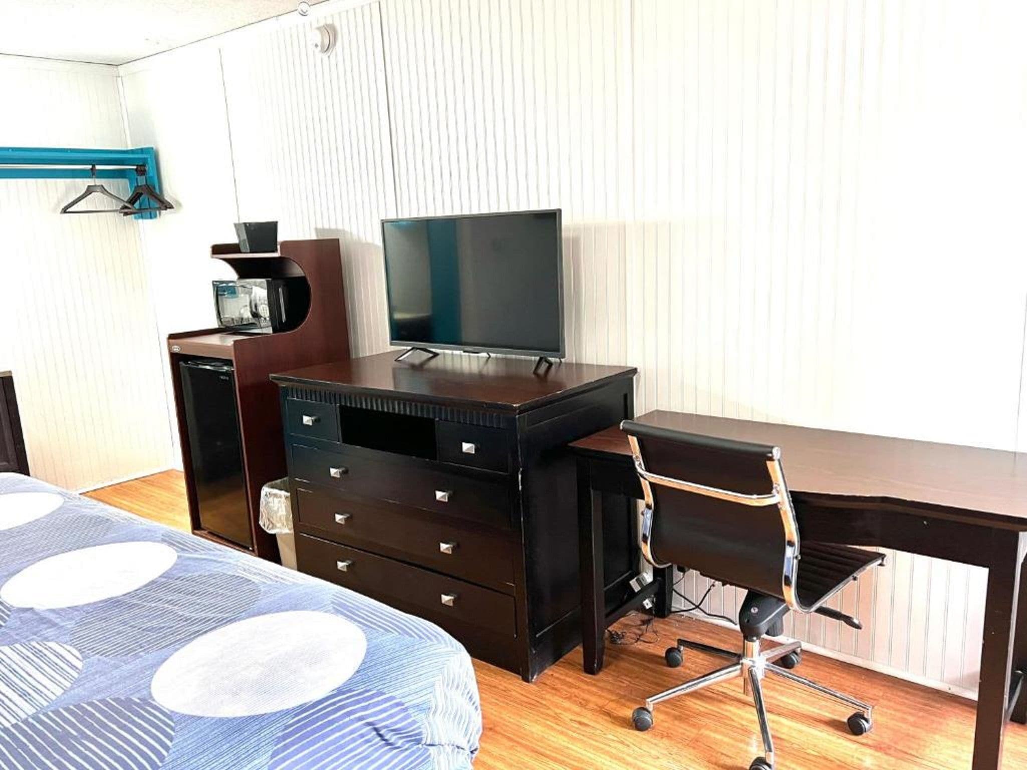 Quarto de hotel com cama, escrivaninha com cadeira, televisão e guarda-roupa.