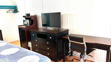 Quarto de hotel com cama, escrivaninha com cadeira, televisão e guarda-roupa.
