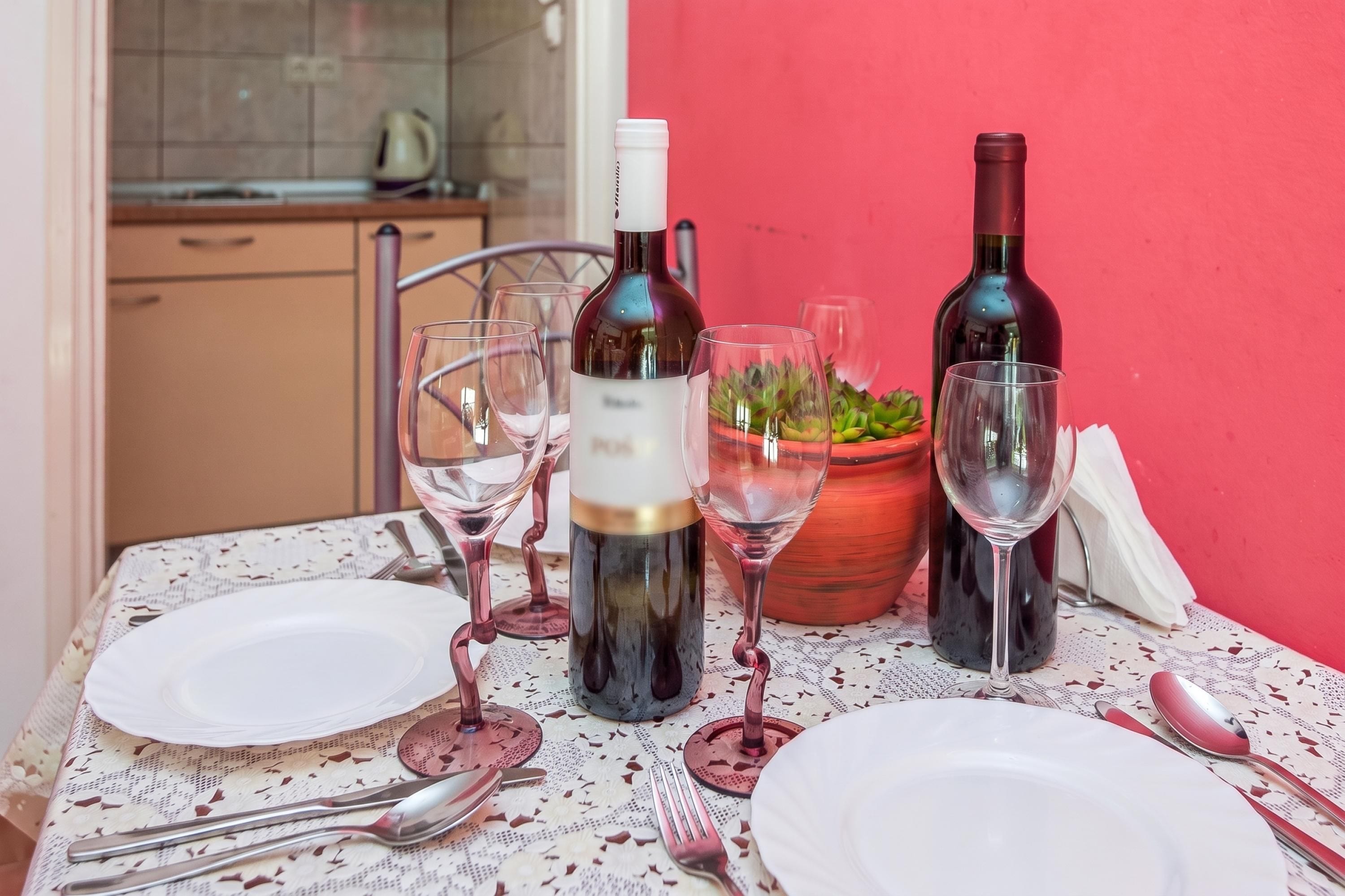 Mesa de jantar posta com copos de vinho, pratos, talheres e um vaso com planta.