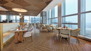 Restaurante moderno com piso de madeira, janelas amplas e teto alto com ripas de madeira.