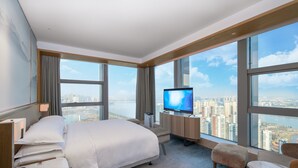 Quarto de hotel moderno com uma cama grande, televisão e vista para a cidade.