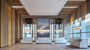 Um lobby moderno com balcão de recepção, área de estar e uma grande obra de arte com vista para a cidade.