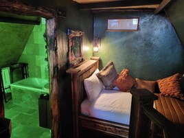Um quarto aconchegante com uma cama de madeira, uma mesa de cabeceira, um espelho e uma pequena janela.
