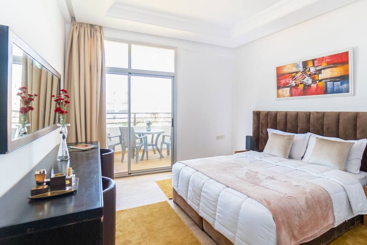 Quarto de hotel com cama, mesa de cabeceira, espelho, quadro e vista para a varanda.