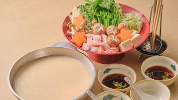 Um conjunto de panela quente com diversos vegetais e carnes, uma tigela de caldo e algumas pequenas tigelas de molho para acompanhar.