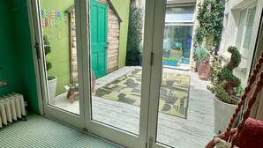 Quarto com uma grande porta de vidro deslizante que dá para um pátio. O quarto possui um tapete listrado, parede verde e uma cadeira suspensa.