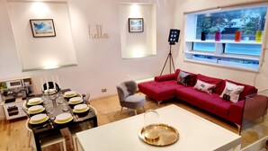 Uma sala de estar moderna com um sofá seccional vermelho, uma mesa de jantar posta com pratos e copos, e uma grande janela com vista para árvores.