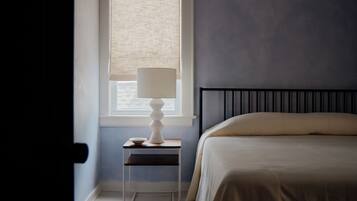 Um quarto com cama, mesa de cabeceira com abajur, janela com vista e porta.