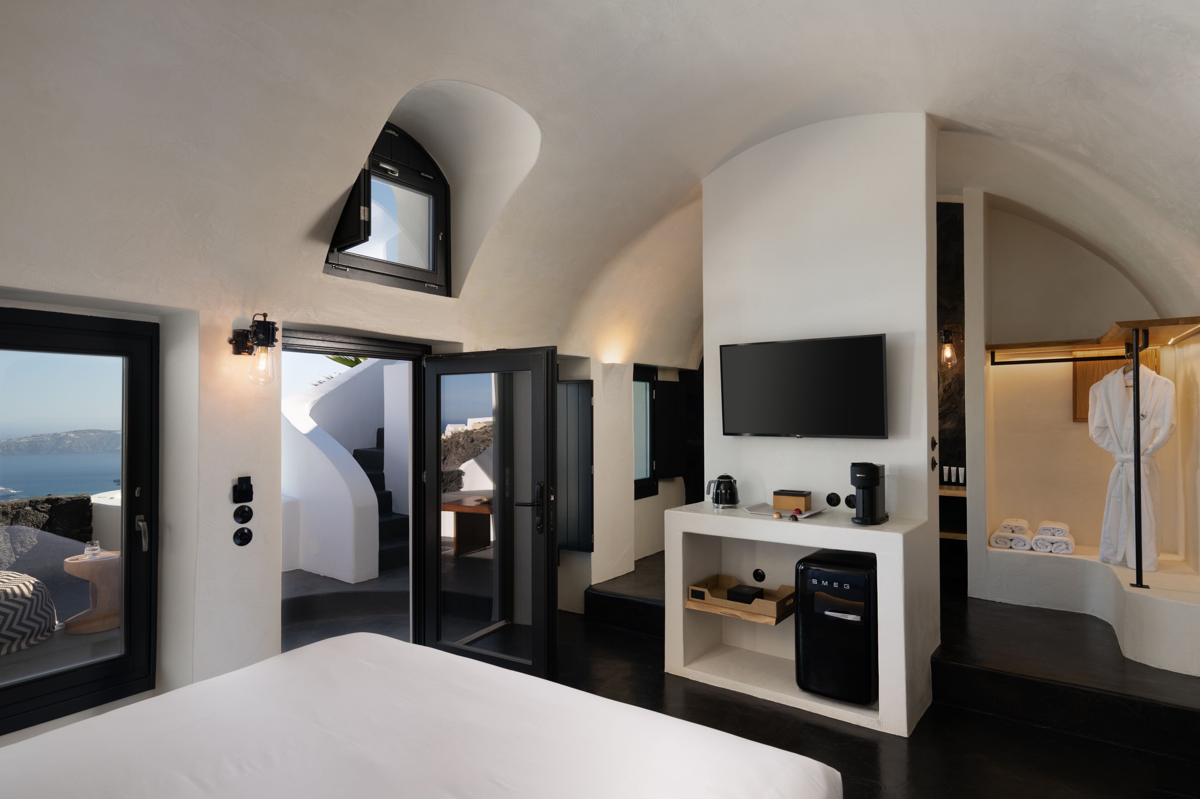 Quarto de hotel moderno com uma cama grande, televisão na parede, máquina de café e vista para o mar.