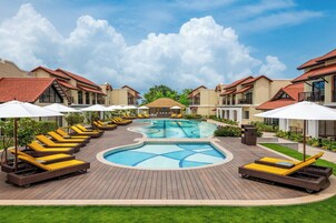 Piscina cercada por espreguiçadeiras e guarda-sóis, com céu claro e edifícios ao fundo.