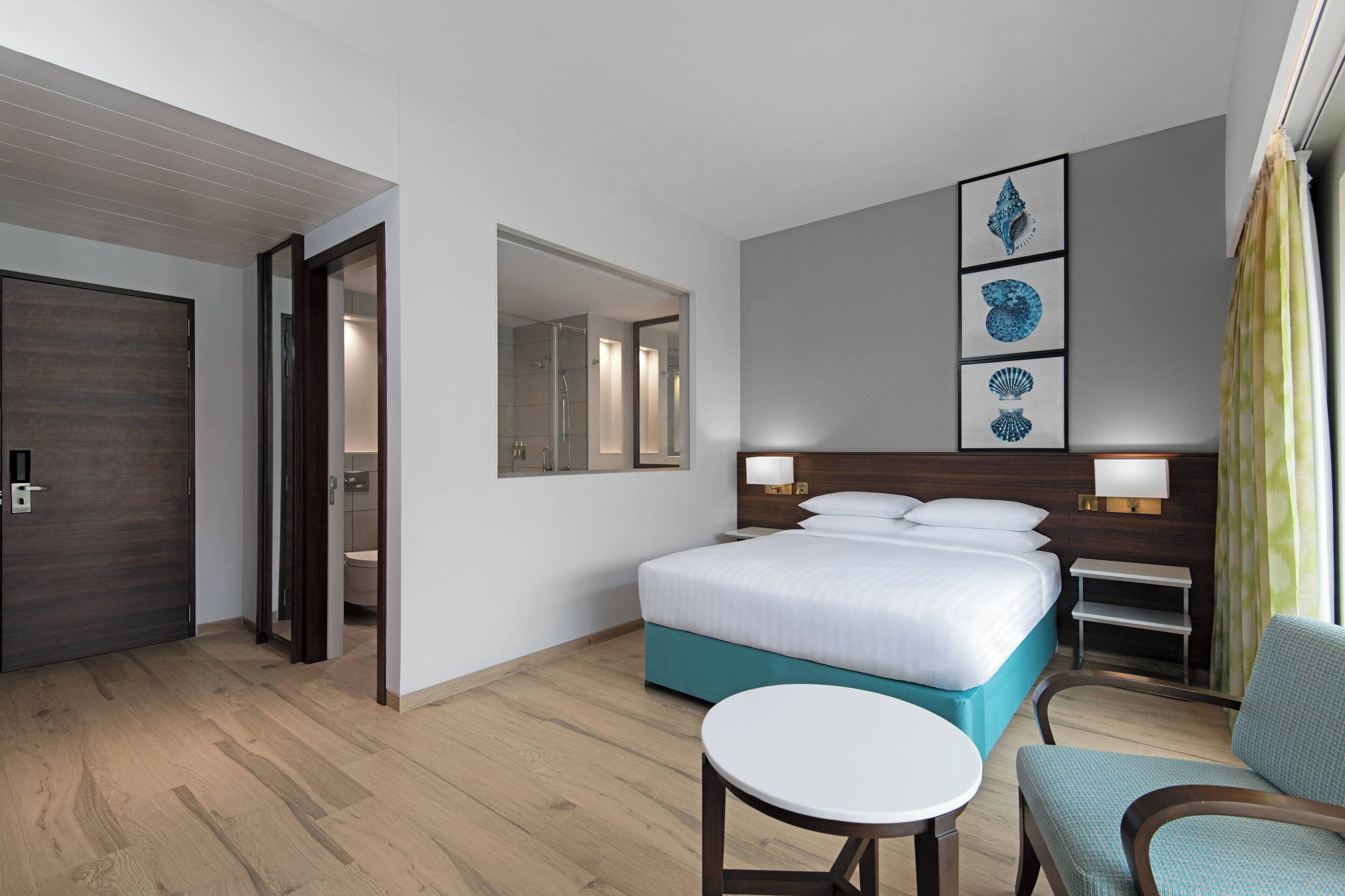 Quarto de hotel com uma cama, mesas de cabeceira, uma cadeira, uma mesinha e obras de arte na parede.