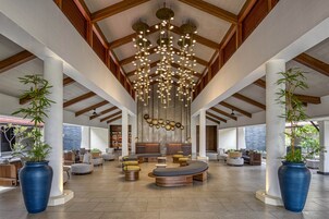 Um hall amplo com teto alto, vigas de madeira e uma área de estar central com vários sofás e poltronas.