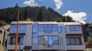 Um edifício moderno de dois andares, com grandes janelas e telhado de metal, com uma paisagem montanhosa arborizada ao fundo.