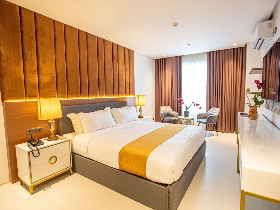 Quarto de hotel moderno com cama grande, luminárias laterais, escrivaninha e vista para a cidade.
