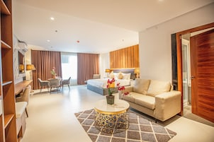 Quarto de hotel moderno com cama, sofá, área de jantar e mesa de centro.