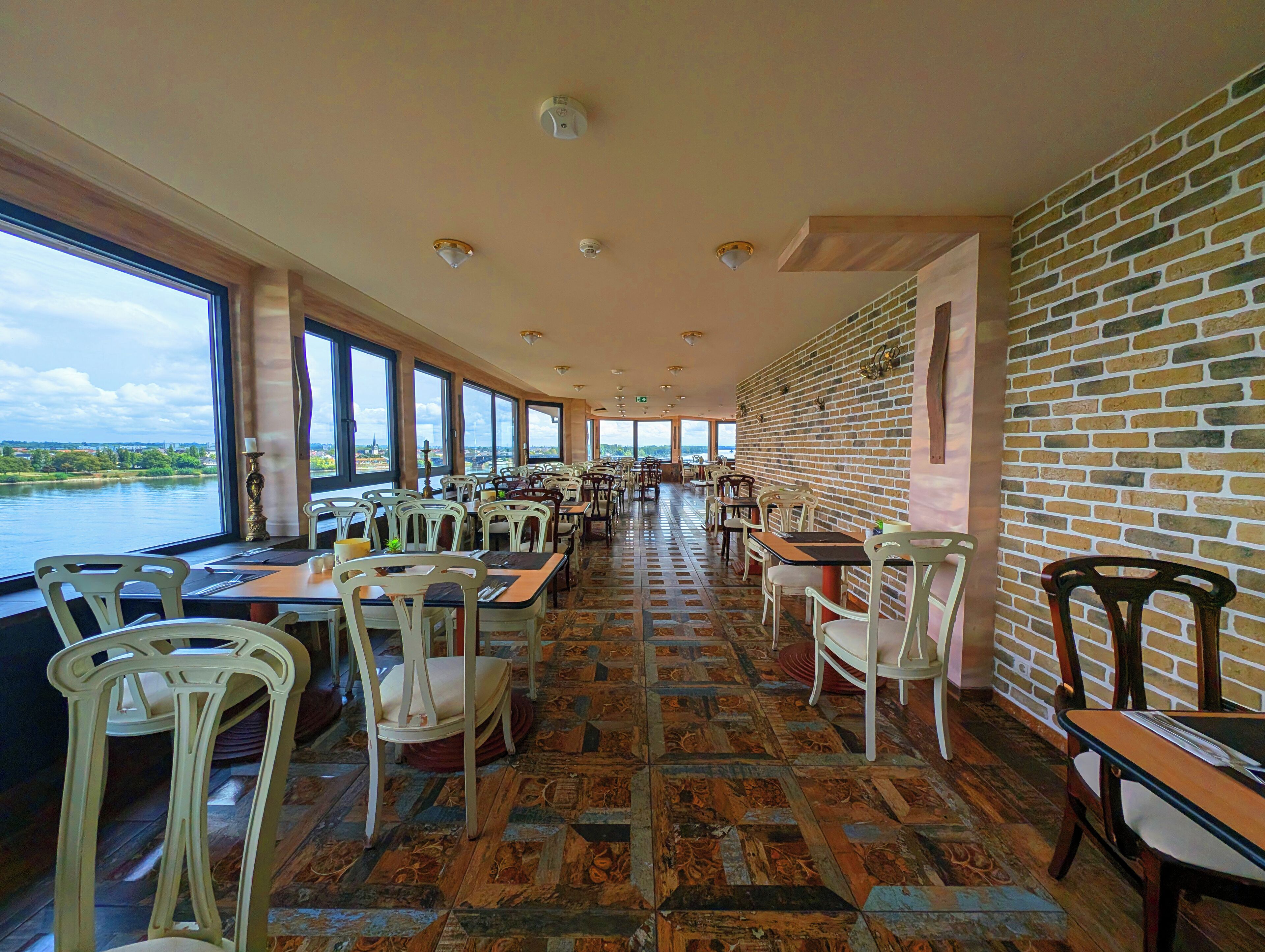 Um restaurante com disposição de mesas longas, grandes janelas e uma parede de tijolos.