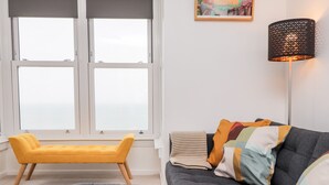 Uma sala de estar moderna com um sofá cinzento, um banco amarelo e um candeeiro de chão.