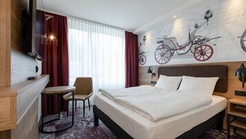 Quarto de hotel com cama, escrivaninha, cadeira, televisão e parede com arte de bicicletas.