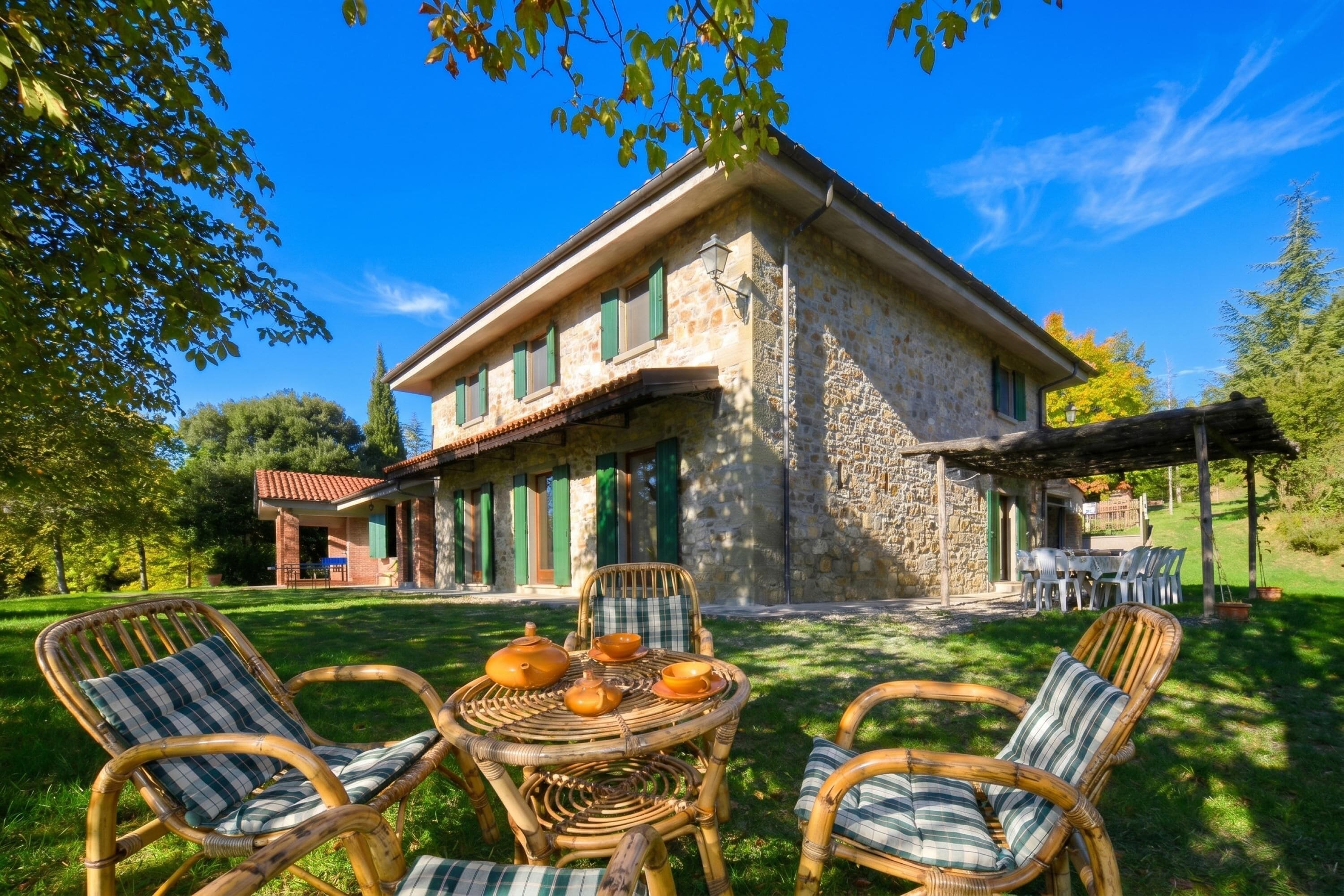 Um edifício de pedra com terraço, cadeiras de vime e uma mesa com bules.