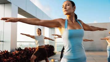 Um grupo de pessoas praticando uma postura de yoga ao ar livre, com um edifício moderno ao fundo.