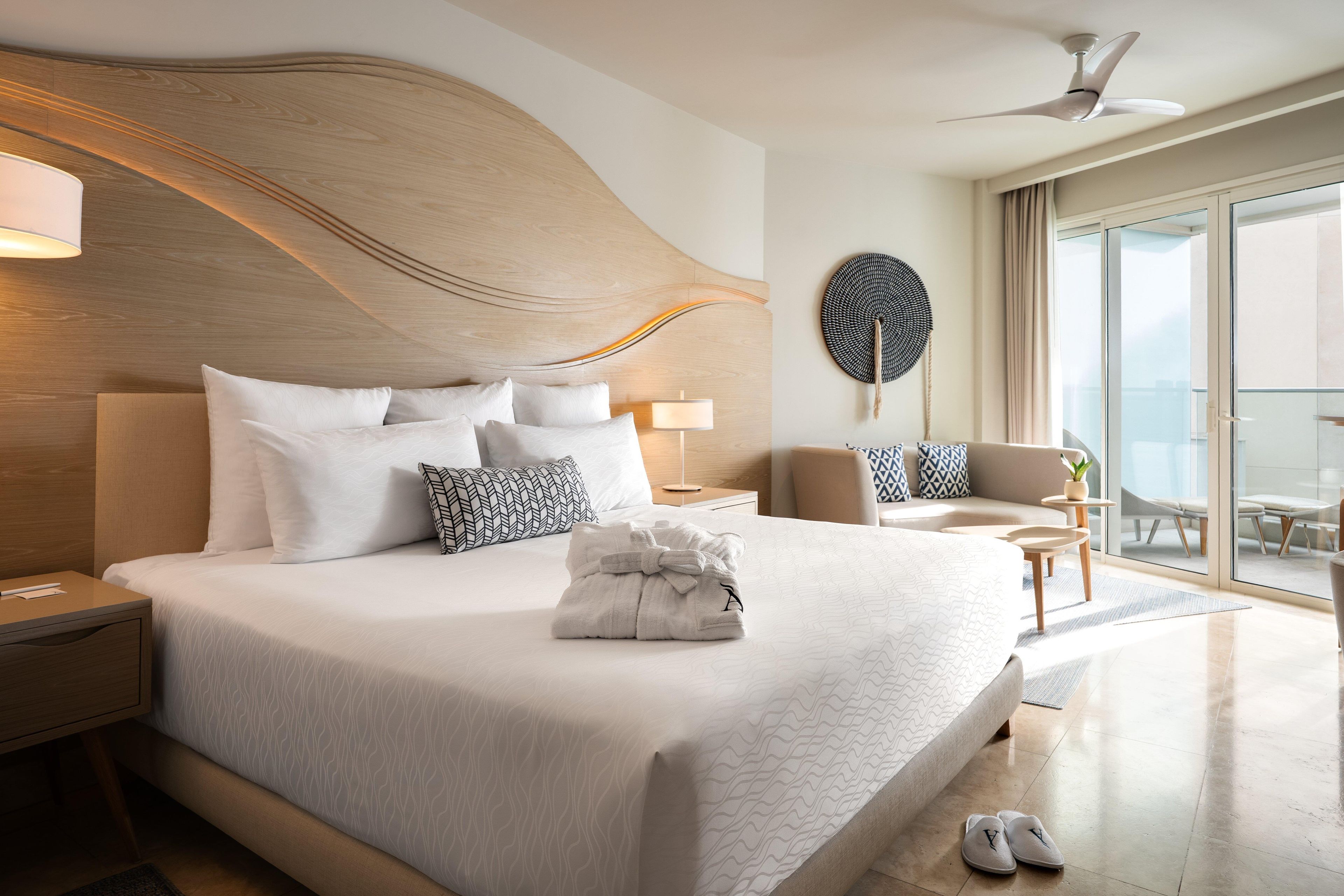 Quarto de hotel com uma cama grande, ventoinha no teto, vista para a cidade e varanda com assentos.
