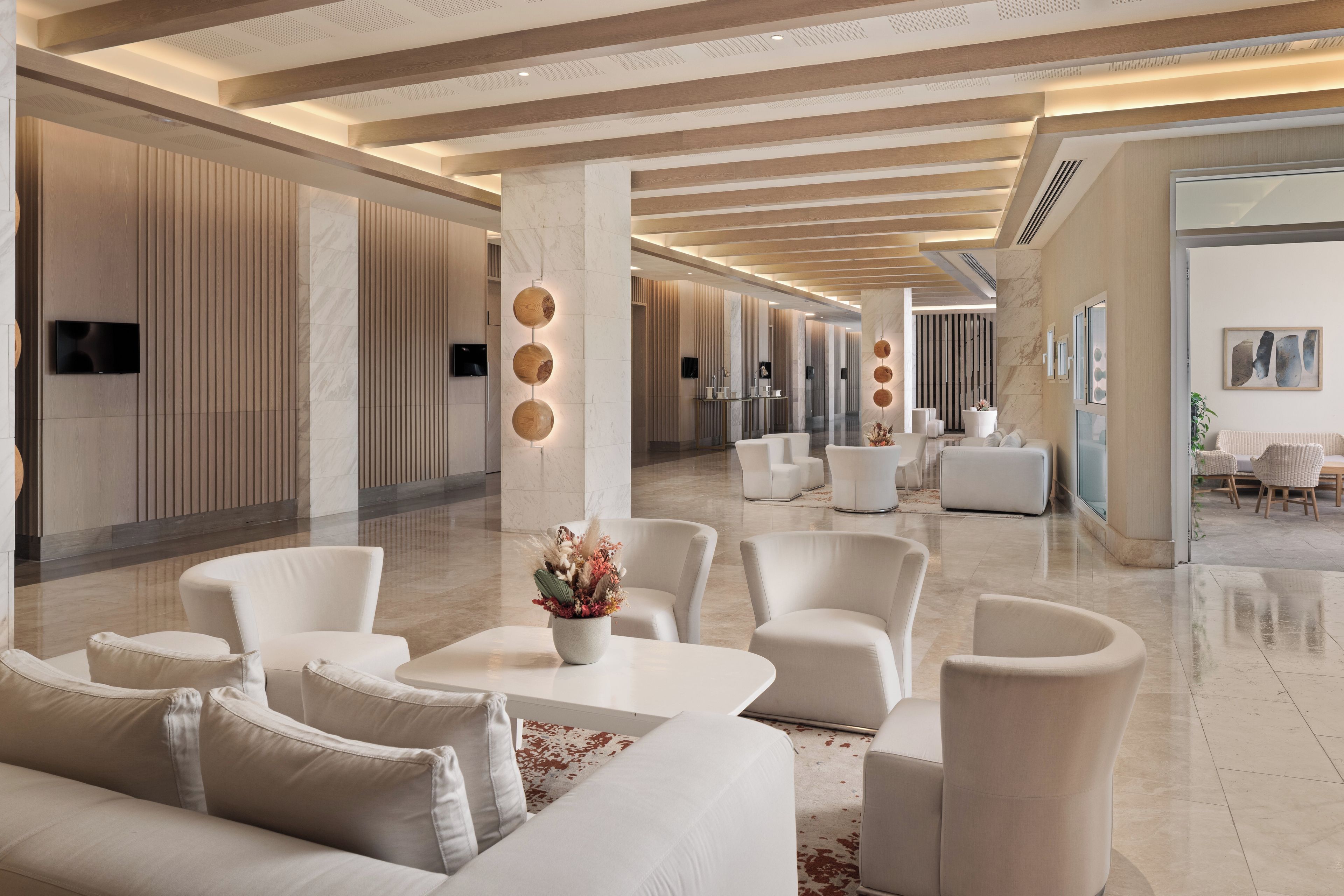Um hall amplo com design moderno, destacando uma mesa de recepção, área de estar e uma grande janela com vista para o exterior.