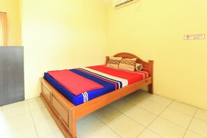 Uma cama de solteiro com cabeceira de madeira, colcha vermelha e azul e travesseiro bege.