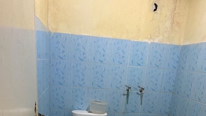 Um banheiro pequeno com vaso sanitário, um balde verde e azulejos com padrão azul.