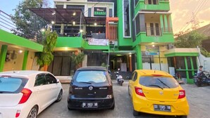 Um edifício de vários andares com fachada verde e branca, uma placa visível para 'BINANGA' e um carro estacionado na frente.