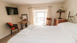 Quarto de hotel com uma cama grande, uma escrivaninha, uma cadeira, televisão e uma janela com cortinas.