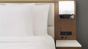 Cama bem arrumada com lençóis brancos, cabeceira de madeira e uma pequena mesa de cabeceira com superfície branca.