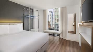 Quarto de hotel moderno com uma cama grande, uma TV, uma escrivaninha e uma janela com vista para a cidade.