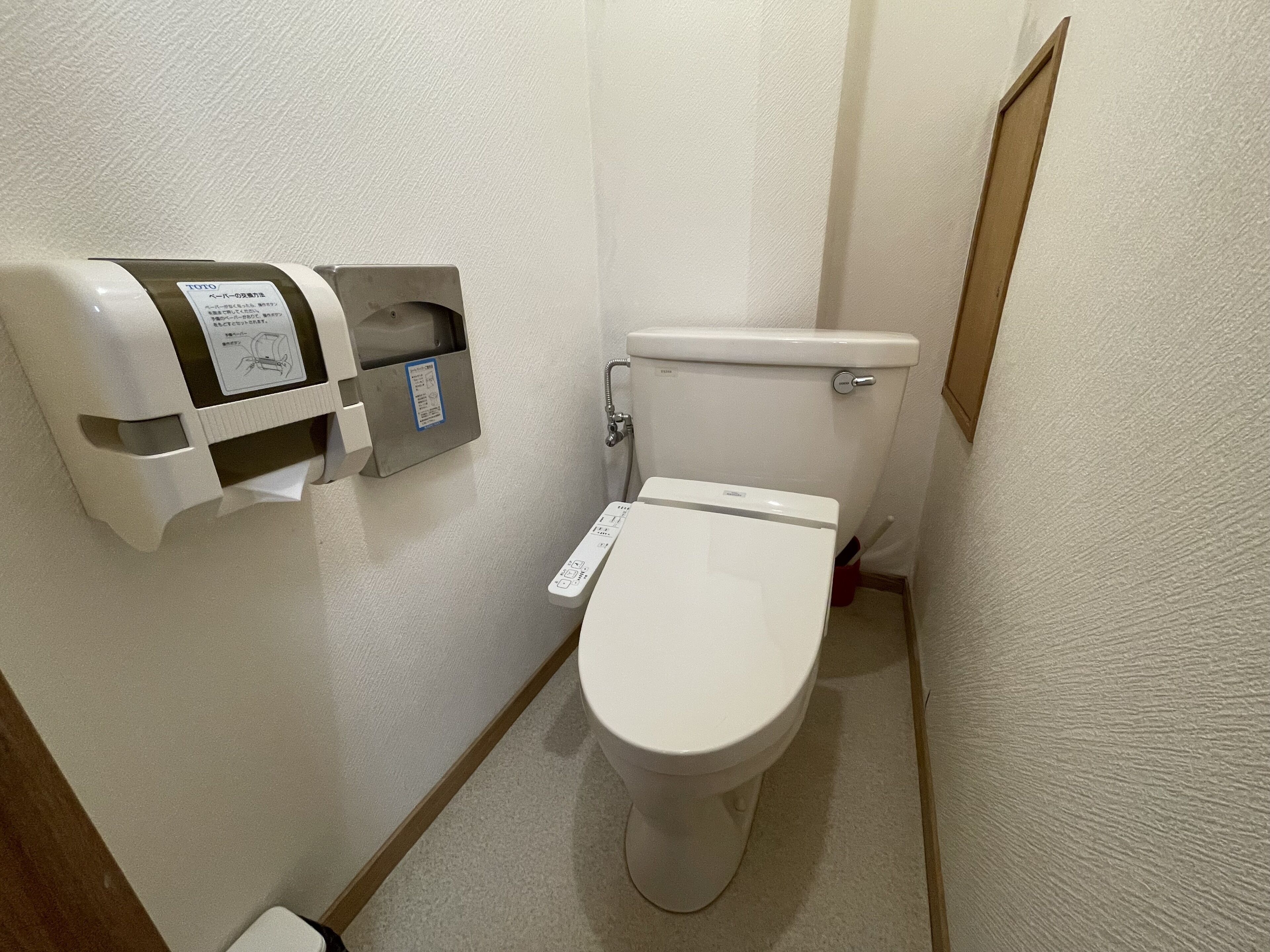 Uma casa de banho pequena e limpa, com sanita, secador de mãos e dispensador de papel.