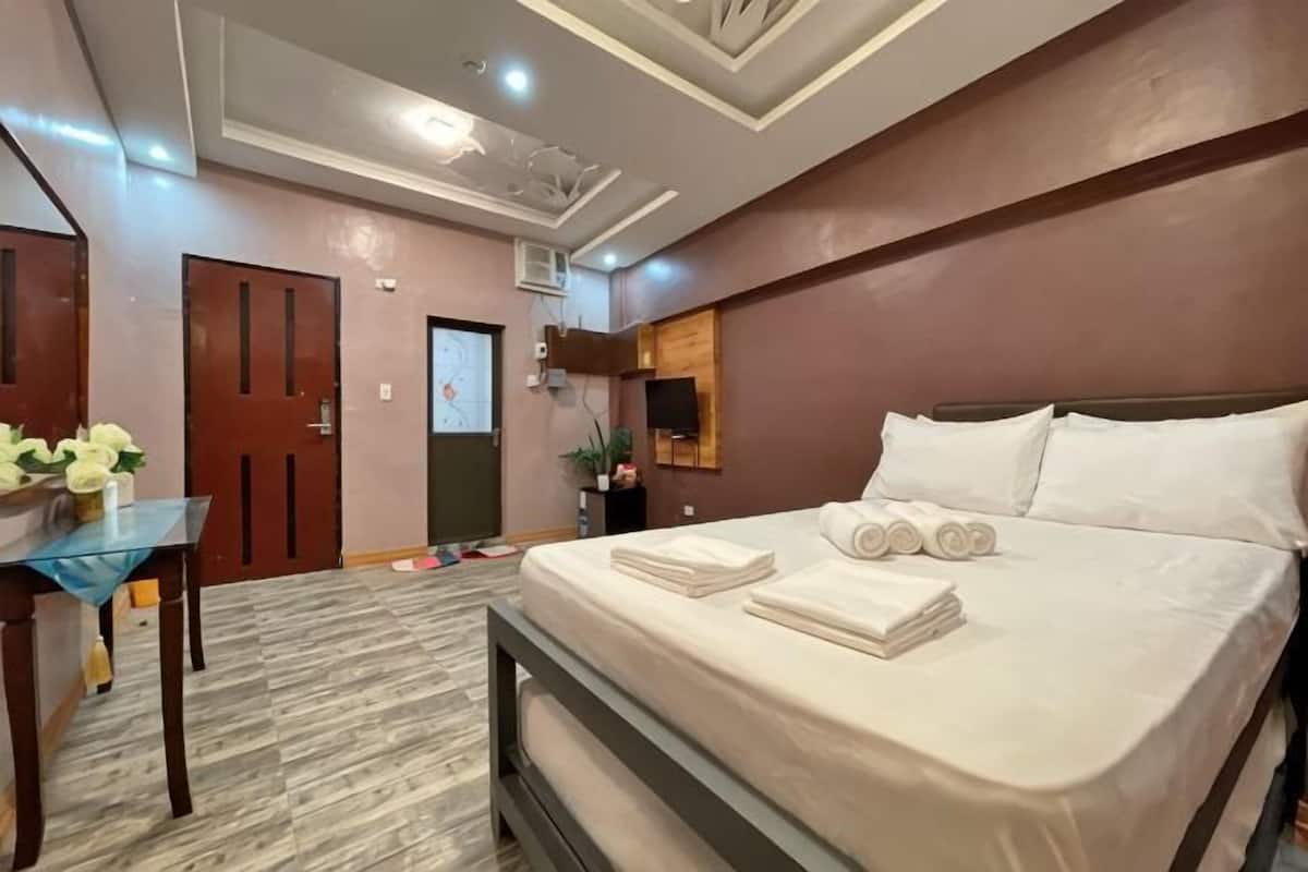 Quarto de hotel com cama, escrivaninha, cadeira, espelho e porta.